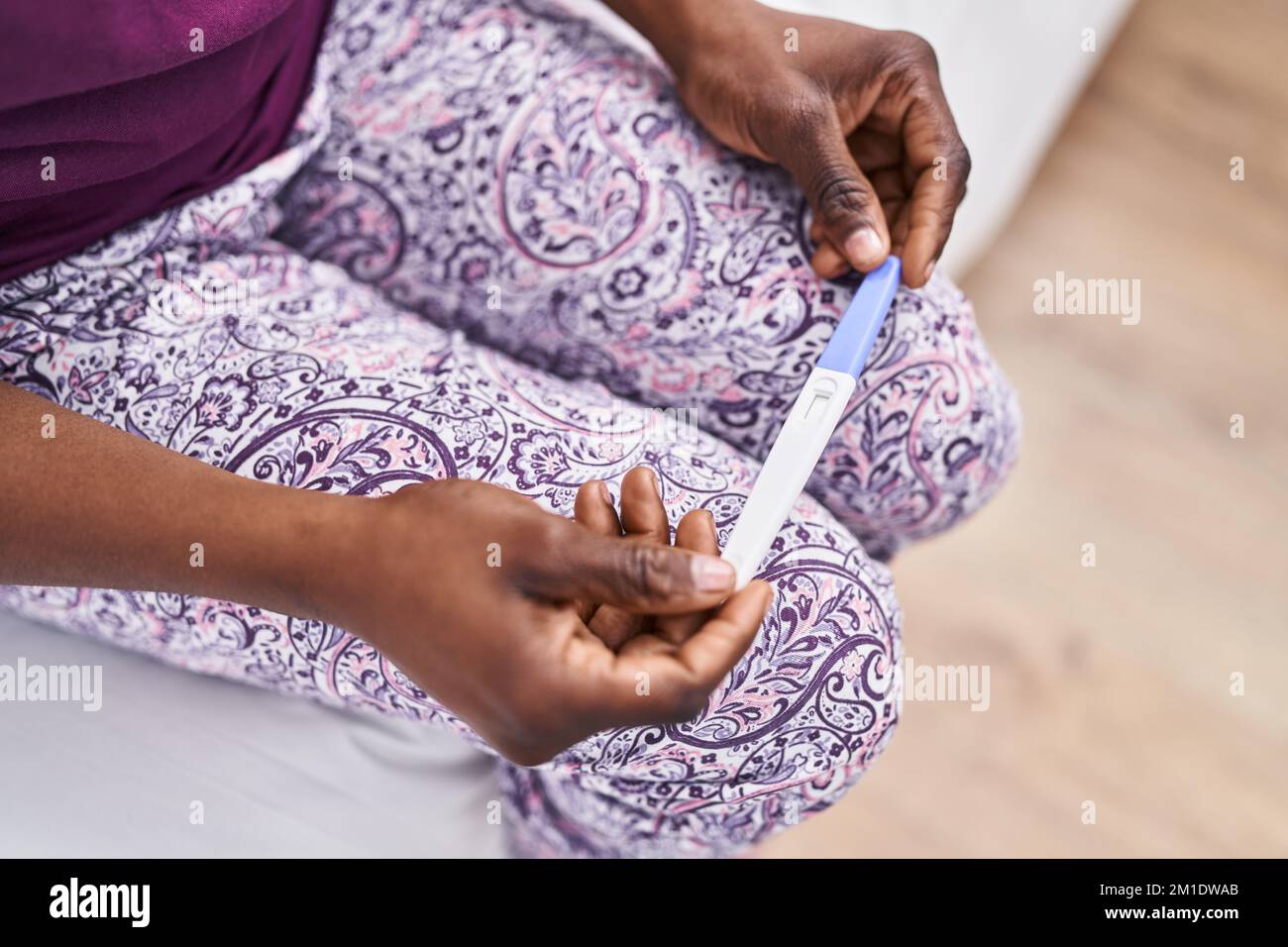 African american woman holding pregnancy test sitting on bed at bedroom ...