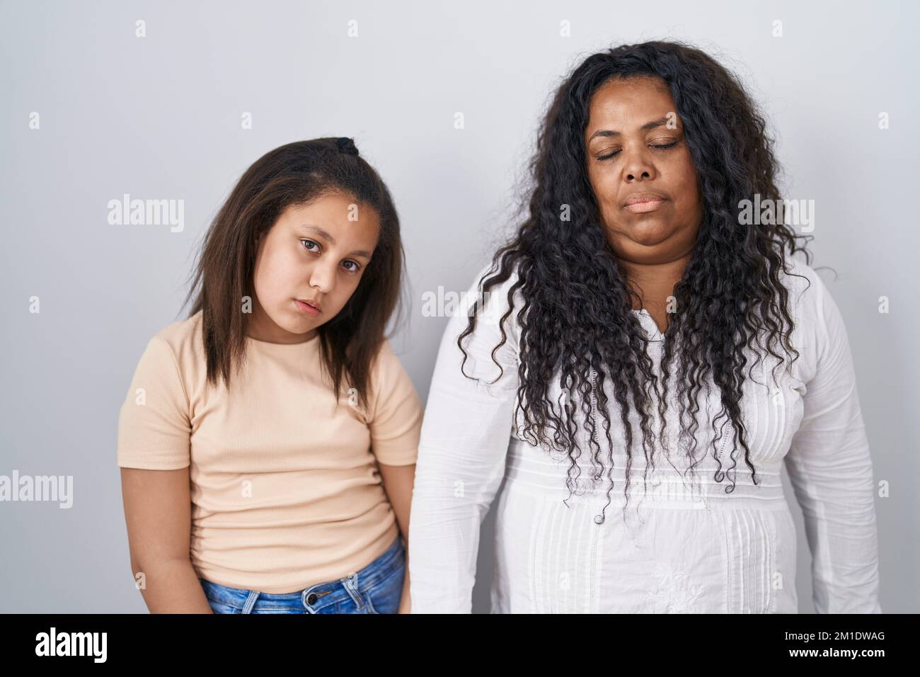 Mother and young daughter standing over white background looking sleepy ...