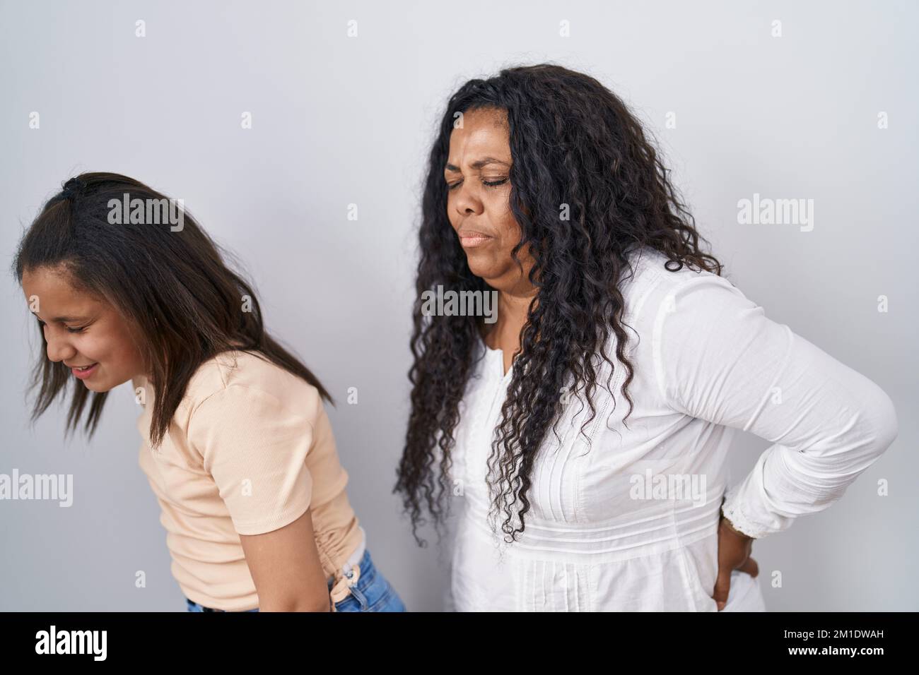 Mother and young daughter standing over white background suffering of ...