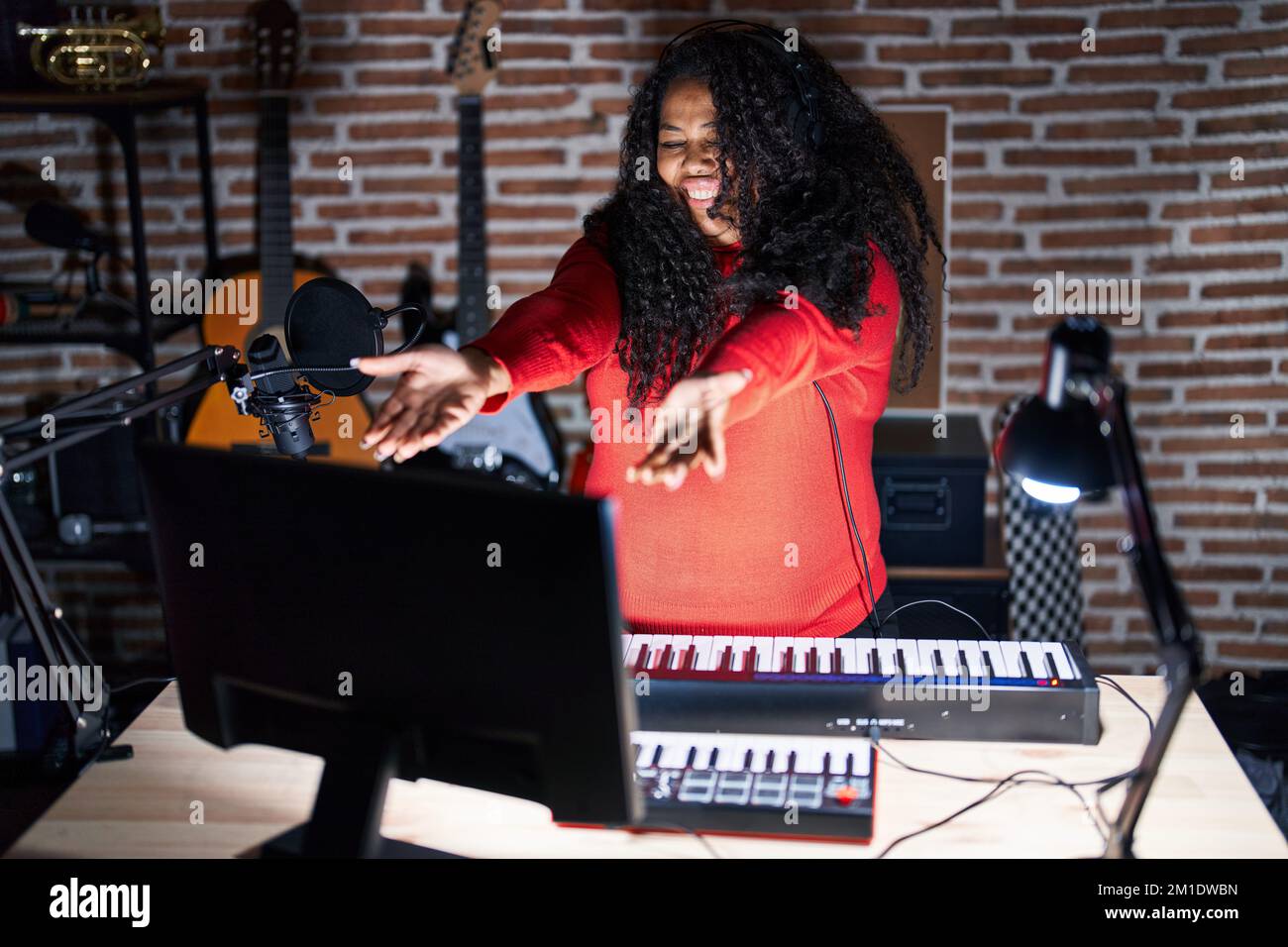 Plus size hispanic woman playing piano at music studio looking at the ...