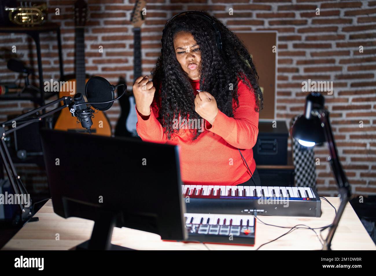 Plus size hispanic woman playing piano at music studio angry and mad ...