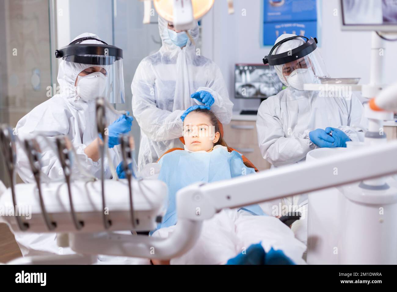 Mother dressed in ppe suit comforting daughter in the course of dental ...