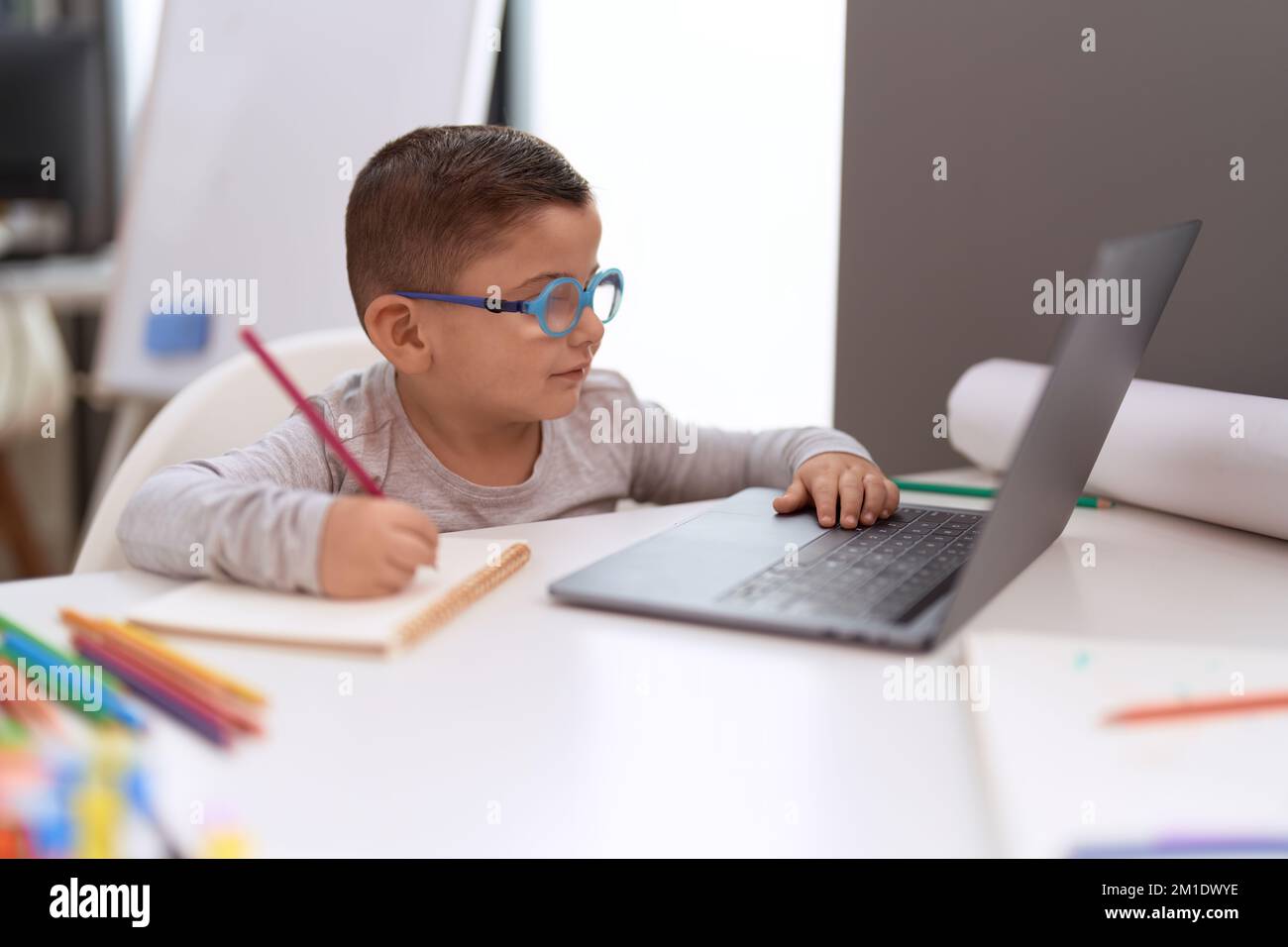 Adorable hispanic toddler student using laptop drawing on notebook at ...