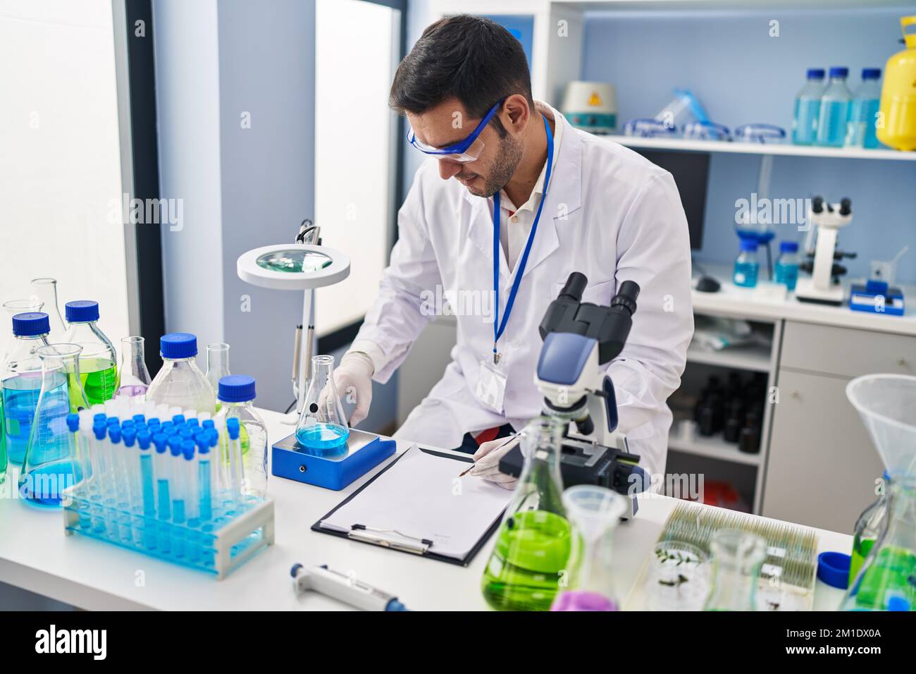 Young hispanic man scientist measuring liquid writing report at ...