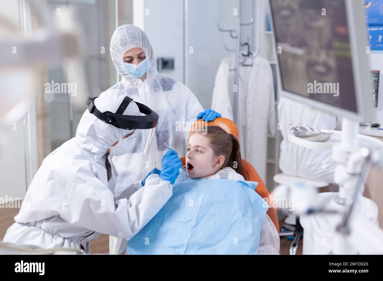 Stomatolog in the course of caries treatment for kid dressed in ppe ...