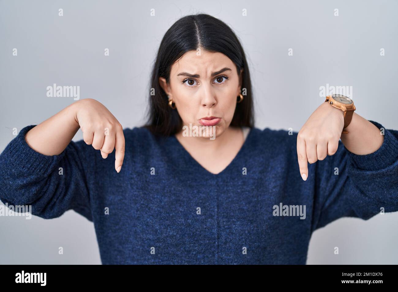 Young brunette woman standing over isolated background pointing down ...
