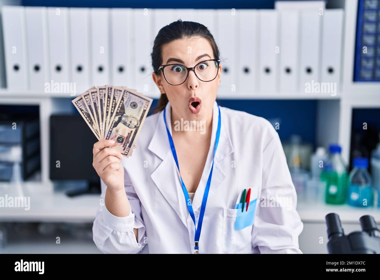 Young brunette woman working at scientist laboratory holding money ...