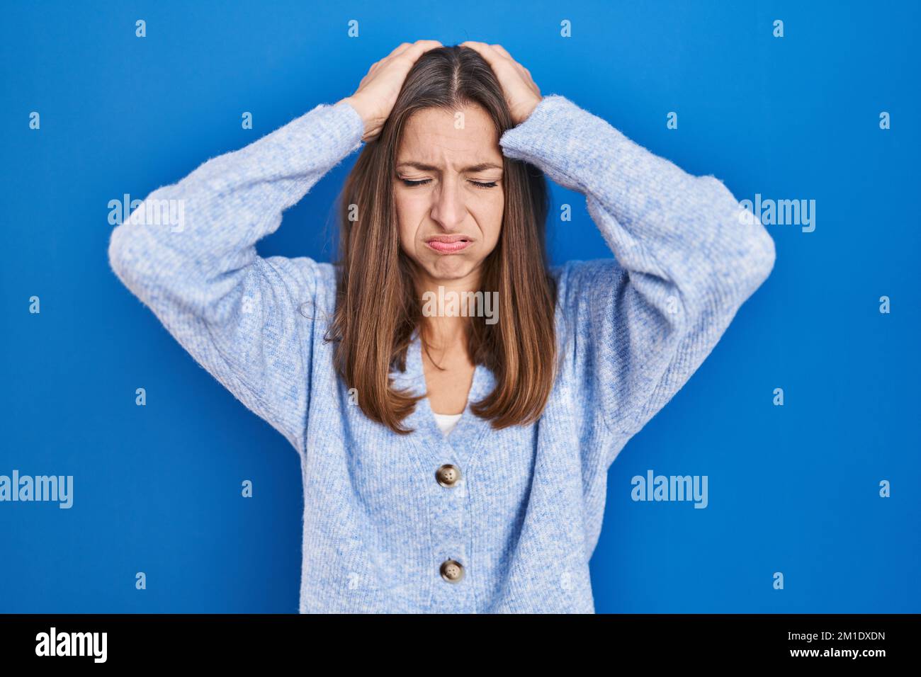 Young woman standing over blue background suffering from headache ...