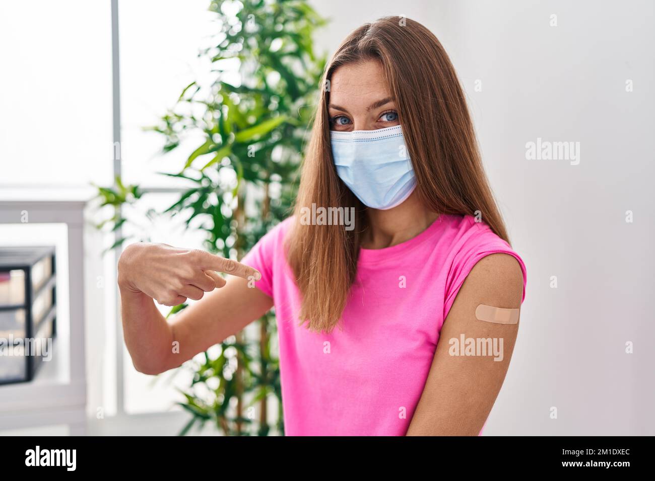 Young woman getting vaccine showing arm with band aid pointing finger ...