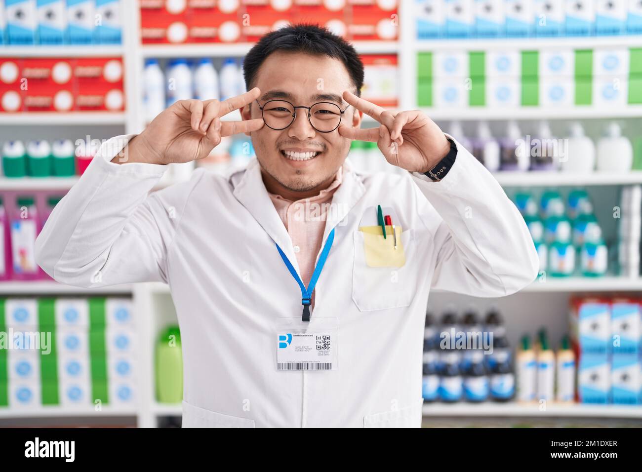 Chinese young man working at pharmacy drugstore doing peace symbol with ...