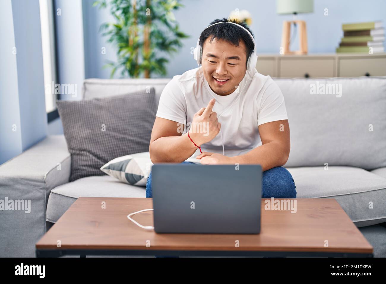Young chinese man using laptop at home smiling happy pointing with hand ...