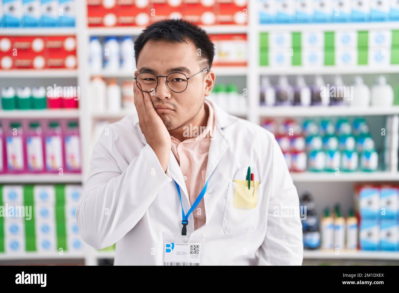 Chinese young man working at pharmacy drugstore thinking looking tired ...