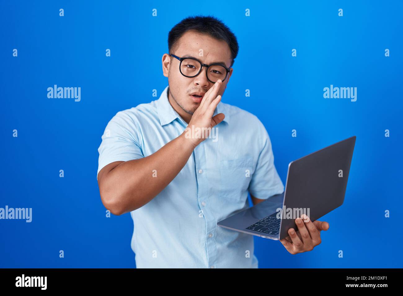 Chinese young man using computer laptop hand on mouth telling secret ...