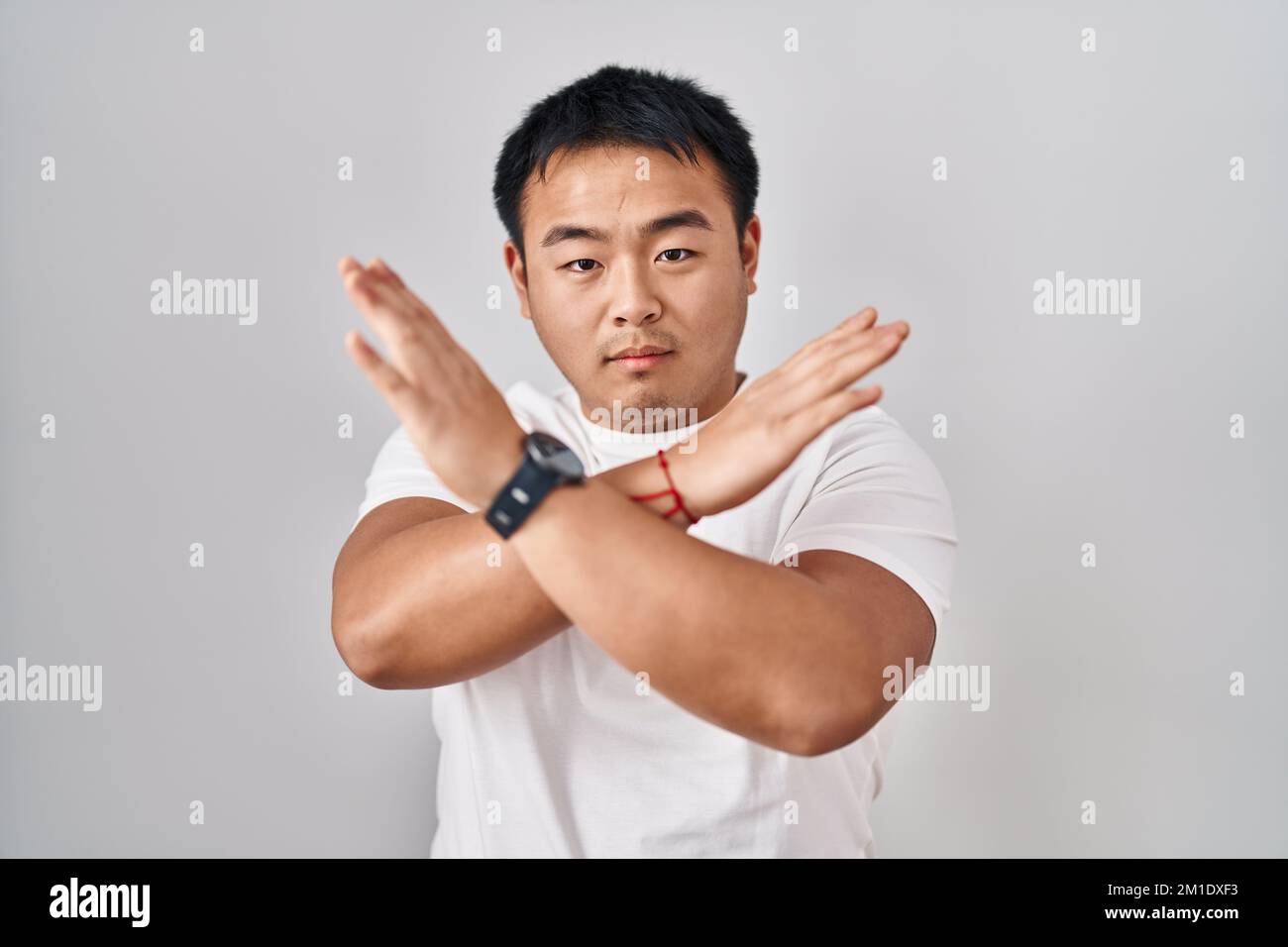 Young chinese man standing over white background rejection expression ...