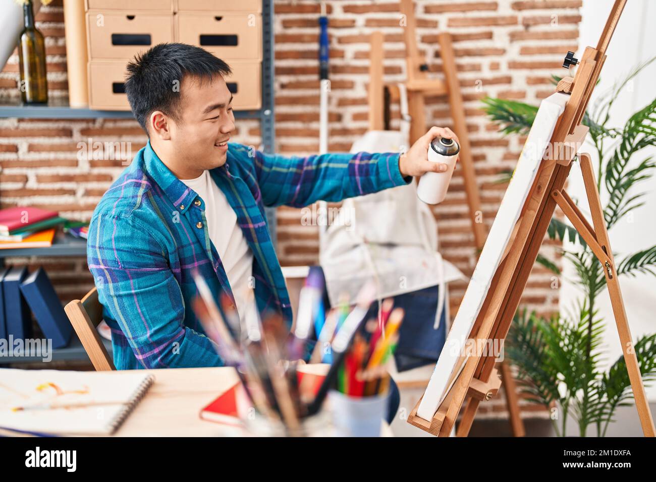 Young chinese man artist drawing on canvas using spray at art studio ...