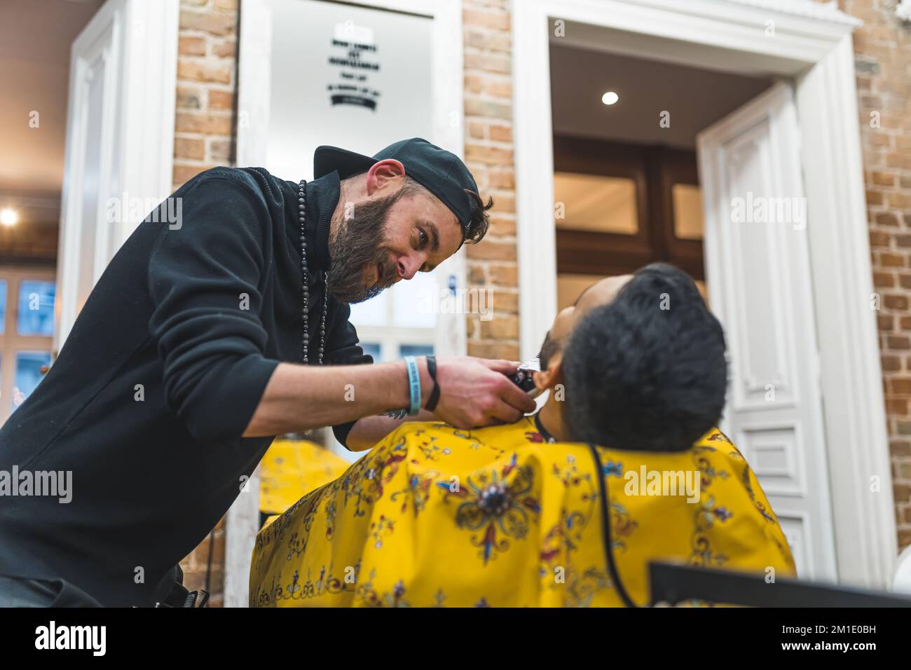 A barber trimming his client beard with an electric shaver. High ...