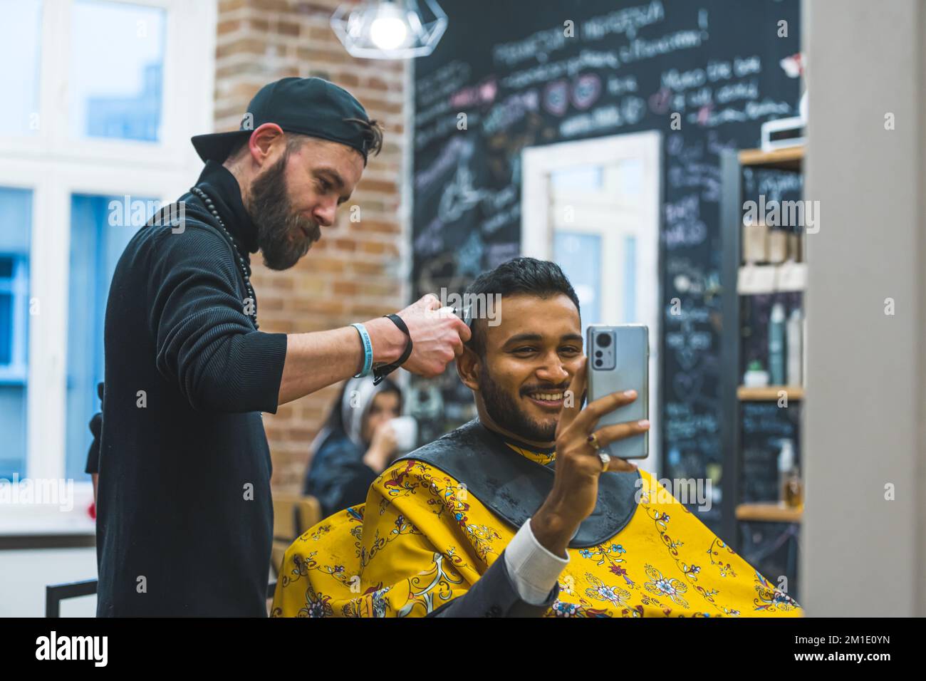 Young man taking mirror selfie while having his hair cut at barber shop ...