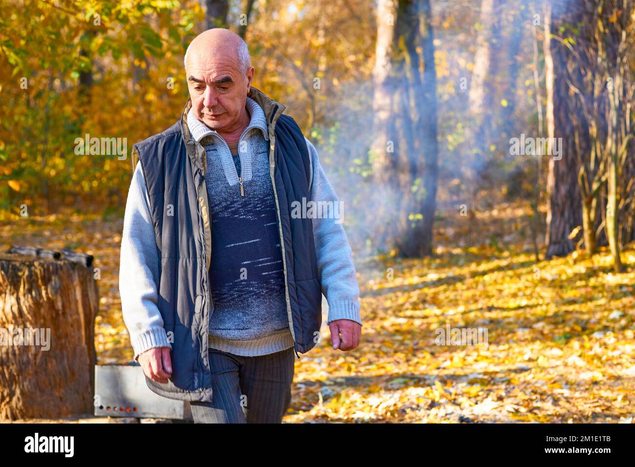 Cheerful elderly man pensioner makes a fire for grilling at a picnic in ...