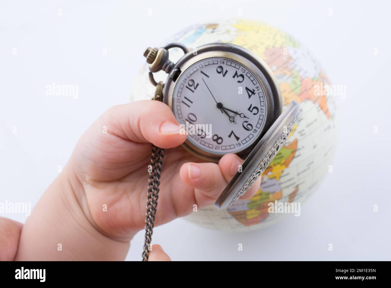 Child holding a pocket watch and a globe in his hand on a white ...