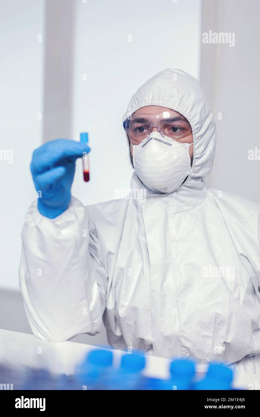 Biochemist in ppe suit looking and working with blood in test tube ...