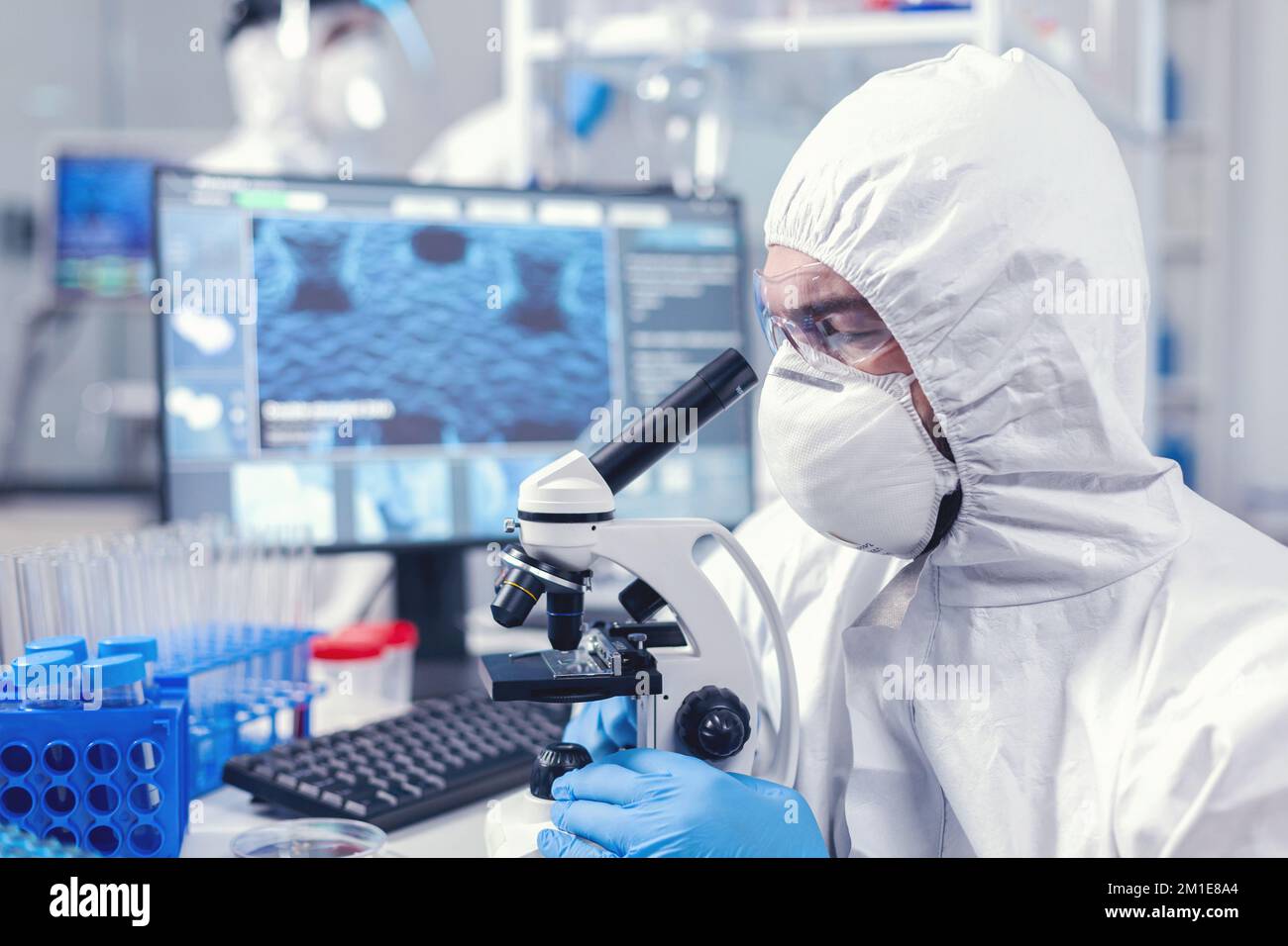 Concentrated scientist in ppe equipment looking into the microscope in ...