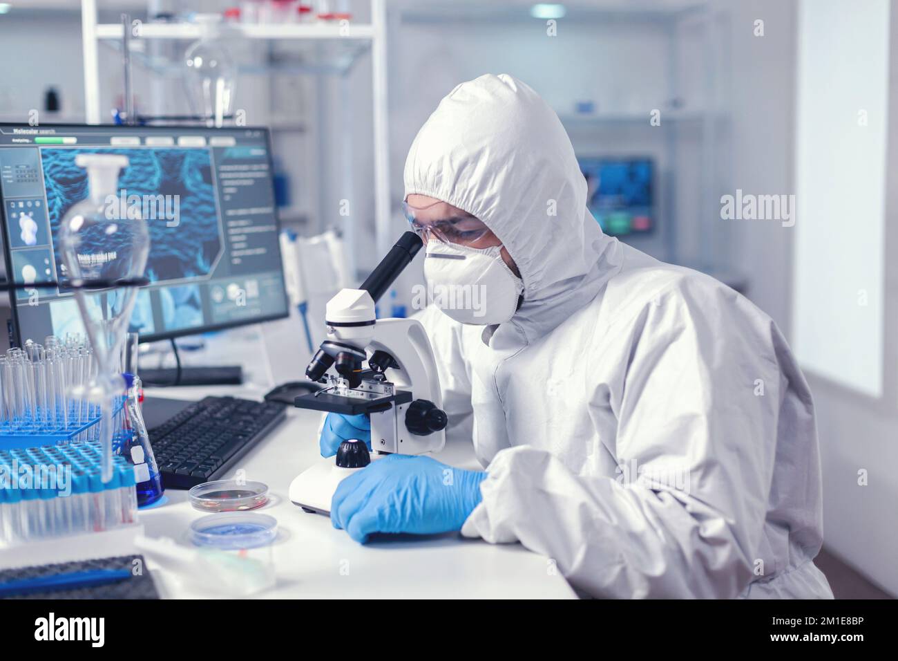 Healthcare specialist analyzing vaccine on microscope dressed in ...