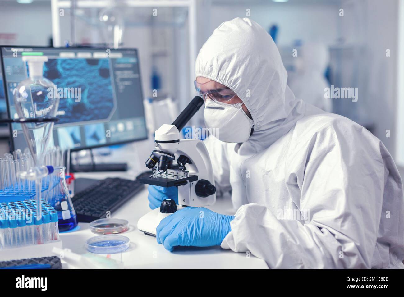 Medic working with microscope analyzing sample using microscope in time of pandemic. Virolog in ...