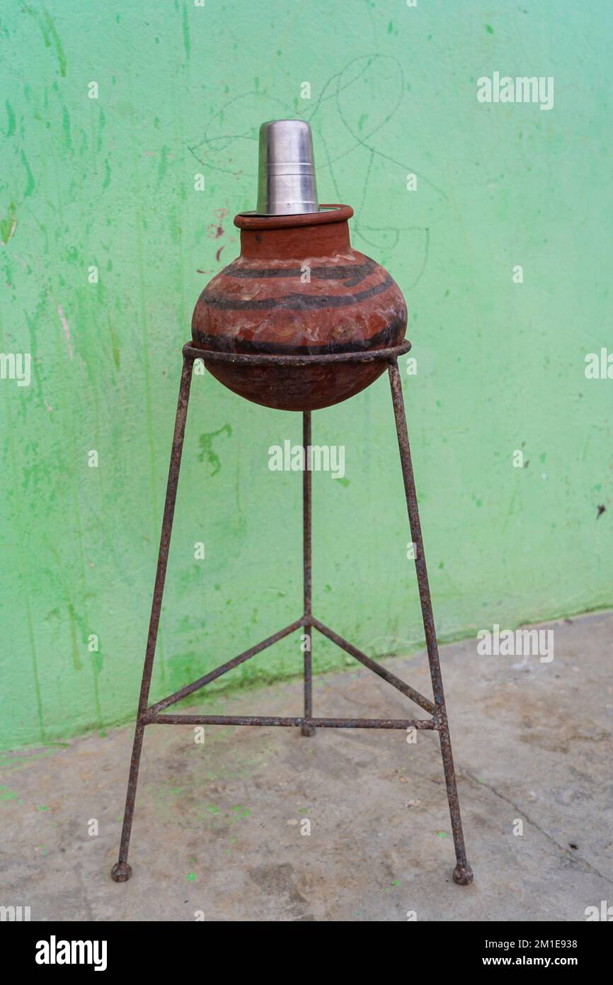 A vertical closeup of a clay Matka on a metal stand with steel glass ...