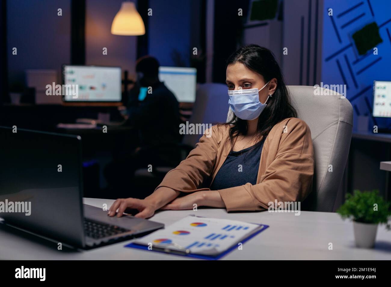 Stressed caucasian young entrepreneur doing overtime wearing face mask ...