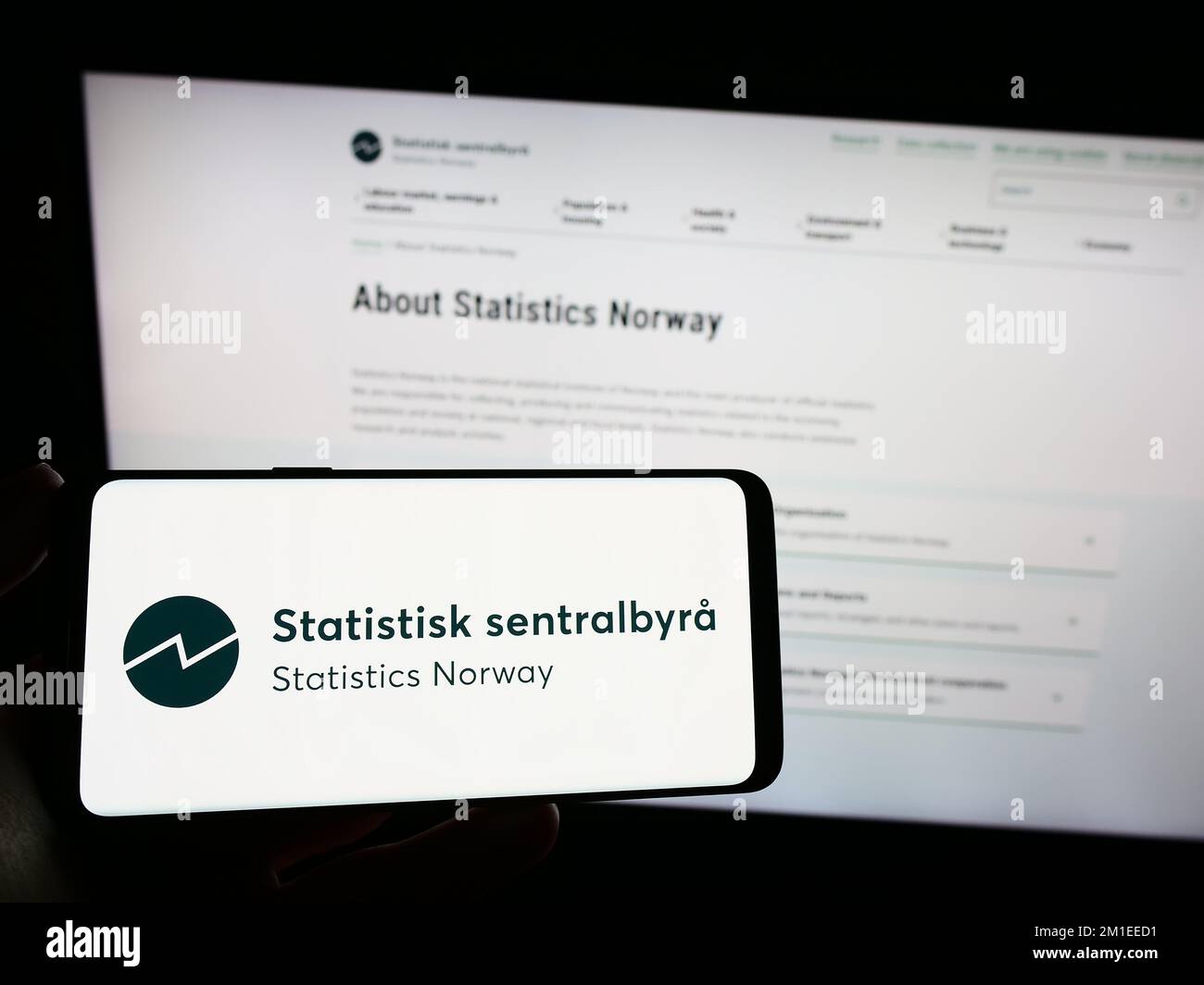 Person holding smartphone with logo of Norwegian agency Statistics ...