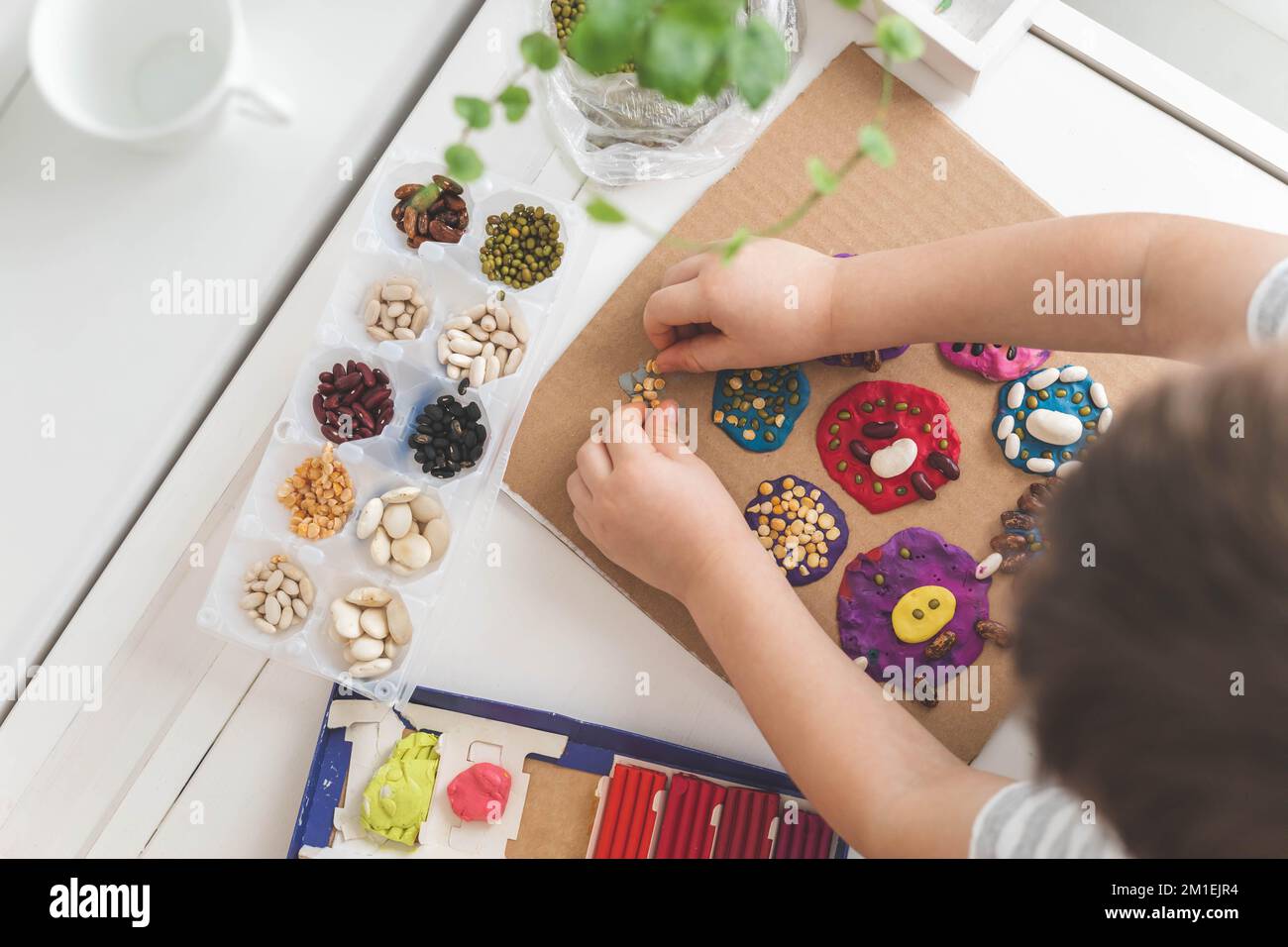 Baby boy creating plasticine diy figure with decorate dried beans ...