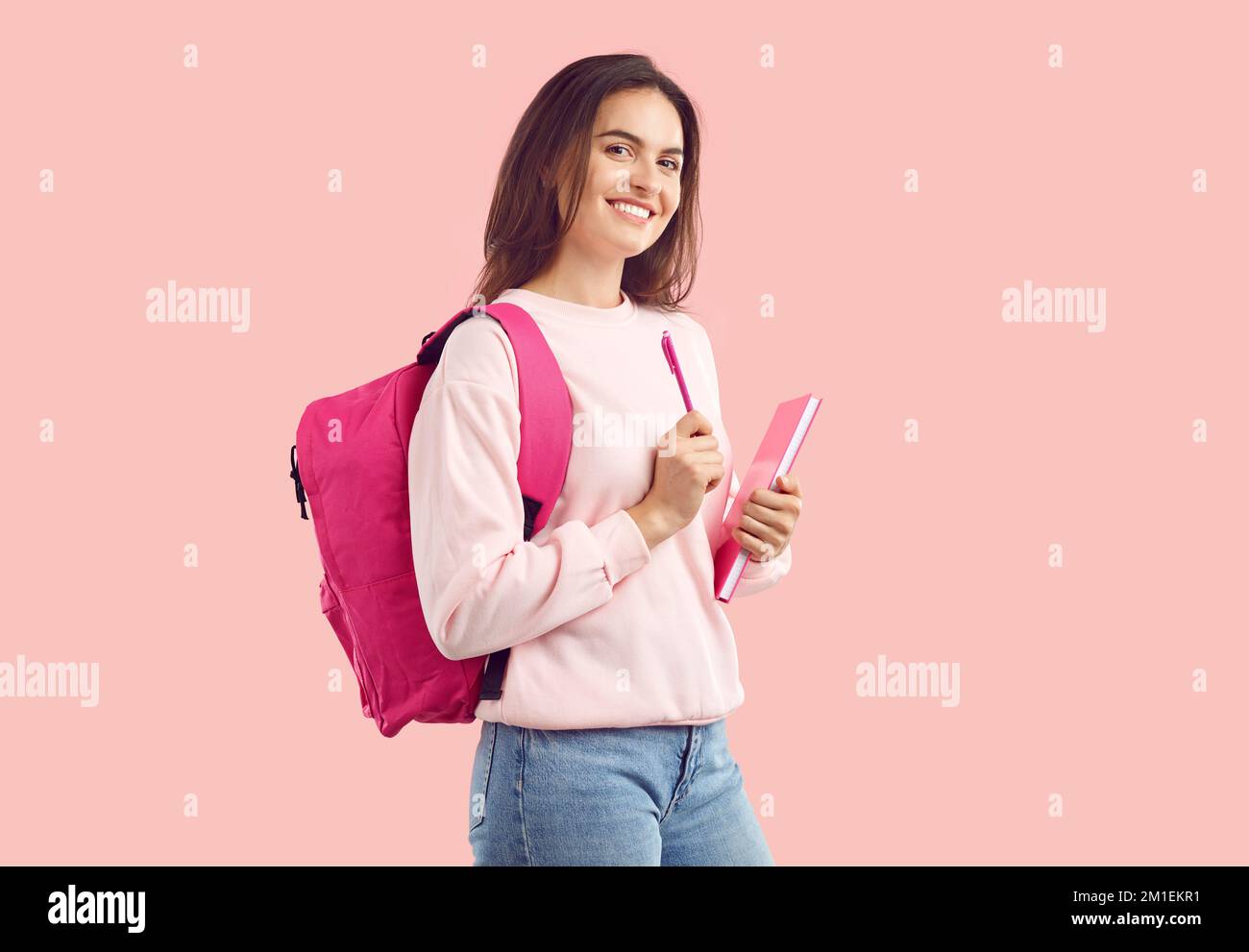 Smiling girl standing with backpack holding study supplies Stock Photo ...