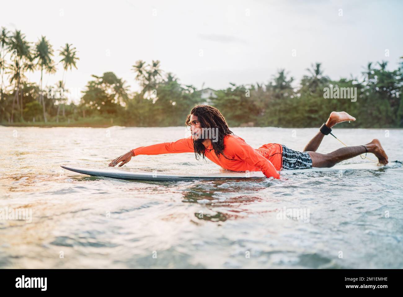 Black long-haired man paddling on long surfboard to the surfing spot in ...