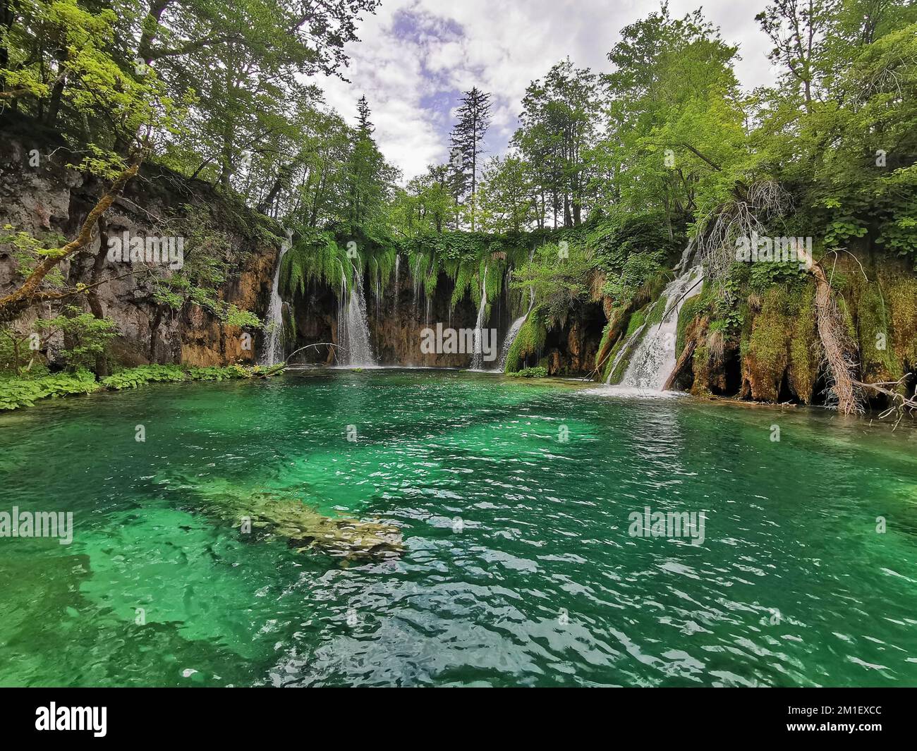 Multiple waterfalls flowing into a clear lake surrounded by green trees ...