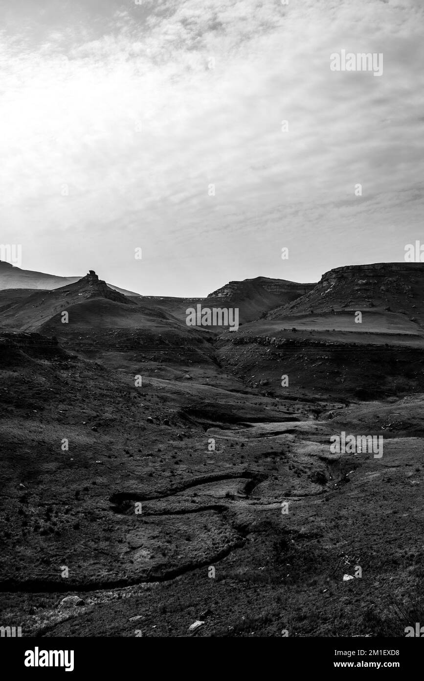 A vertical grayscale of hills in a wilderness under the clouds and sky ...