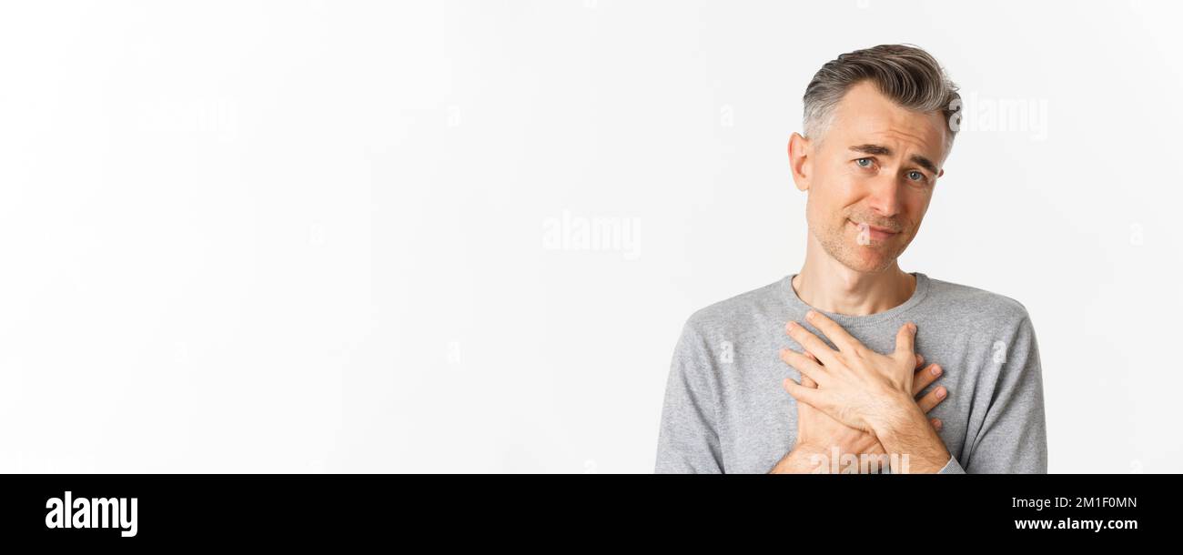 Close-up of thankful middle-aged man, holding hands on heart and ...