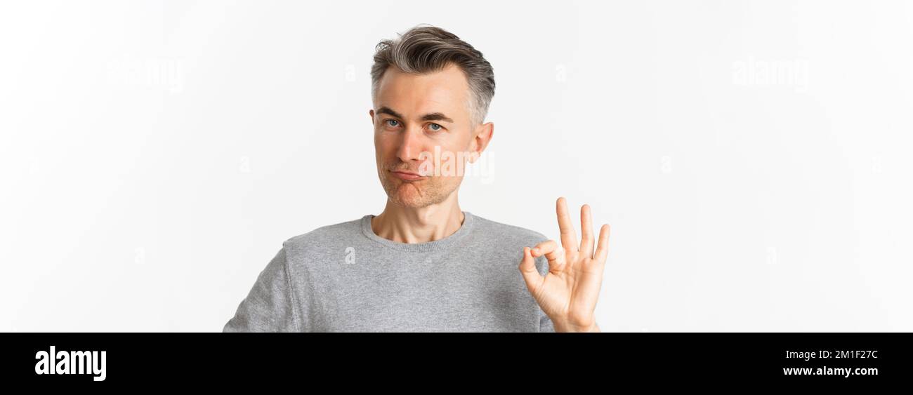 Close-up of satisfied middle-aged man in gray sweater, showing okay ...