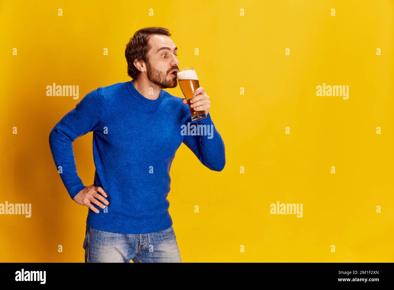 Portrait of mature man in blue sweater posing with beer glass, sipping ...