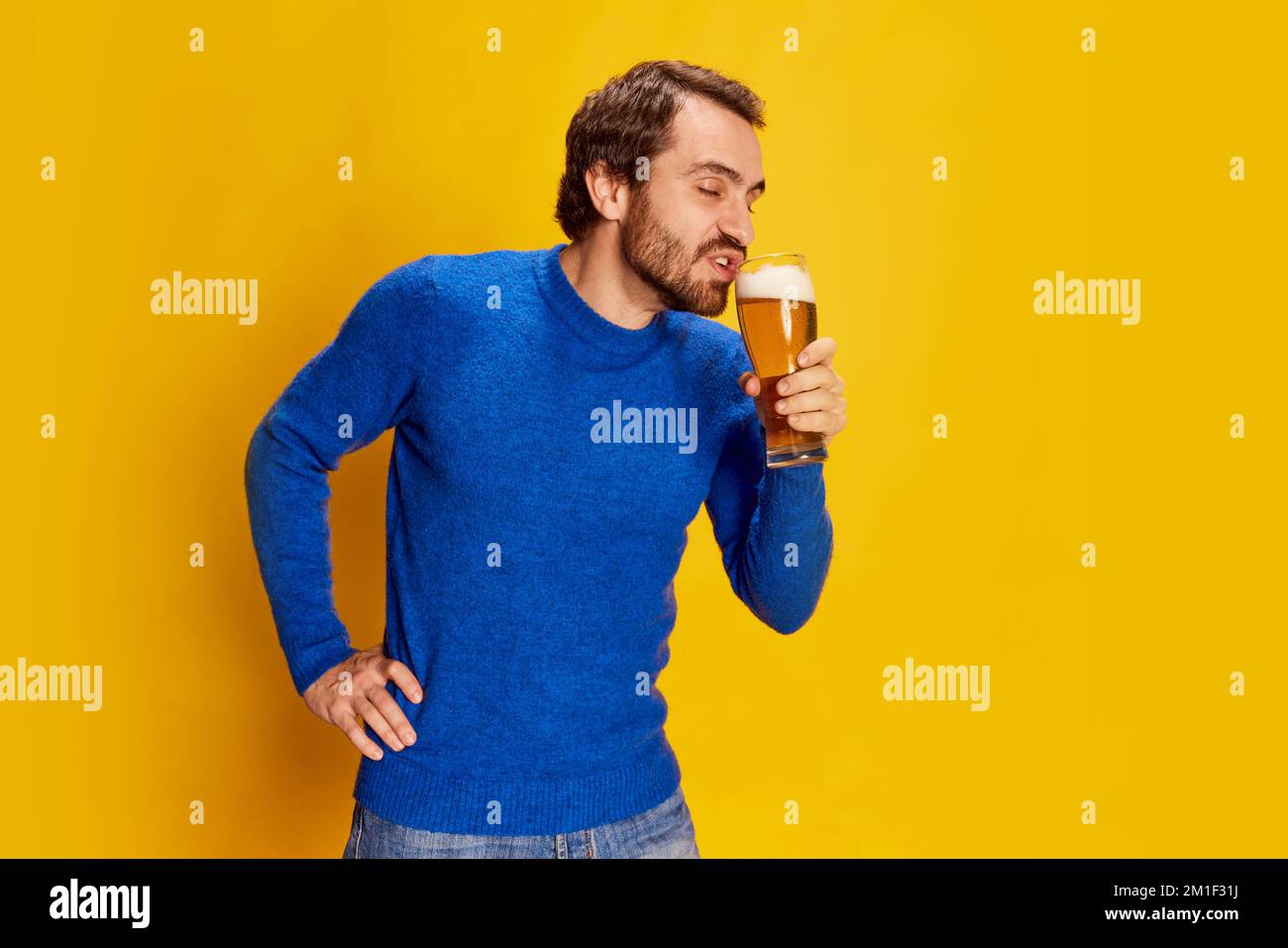 Portrait of emotive man in blue sweater posing with beer mug, drinking ...