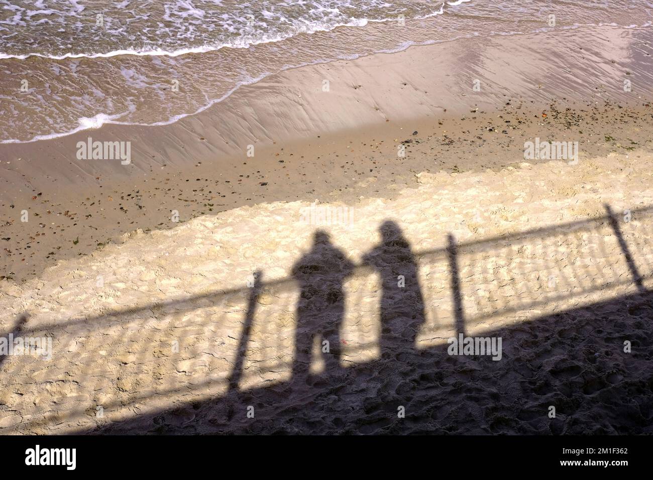 Shadow on the beach sand of two loving people, standing near parapet ...