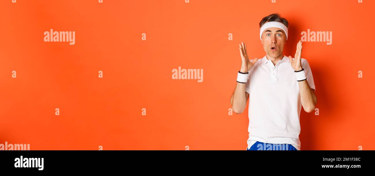 Portrait of surprised senior sportsman gasping amazed, raising hands up ...