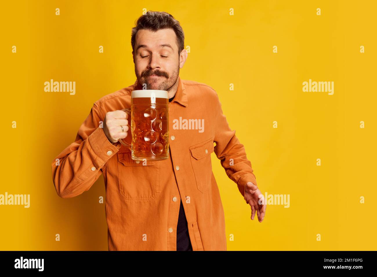 Portrait of emotive handsome man in orange shirt posing with lager ...