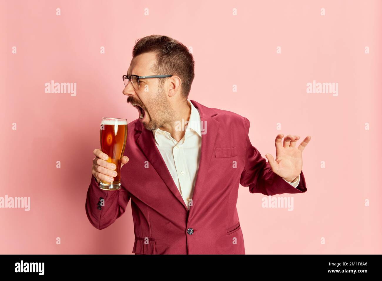 Portrait of stylish emotive man in a suit posing with glass of lager ...