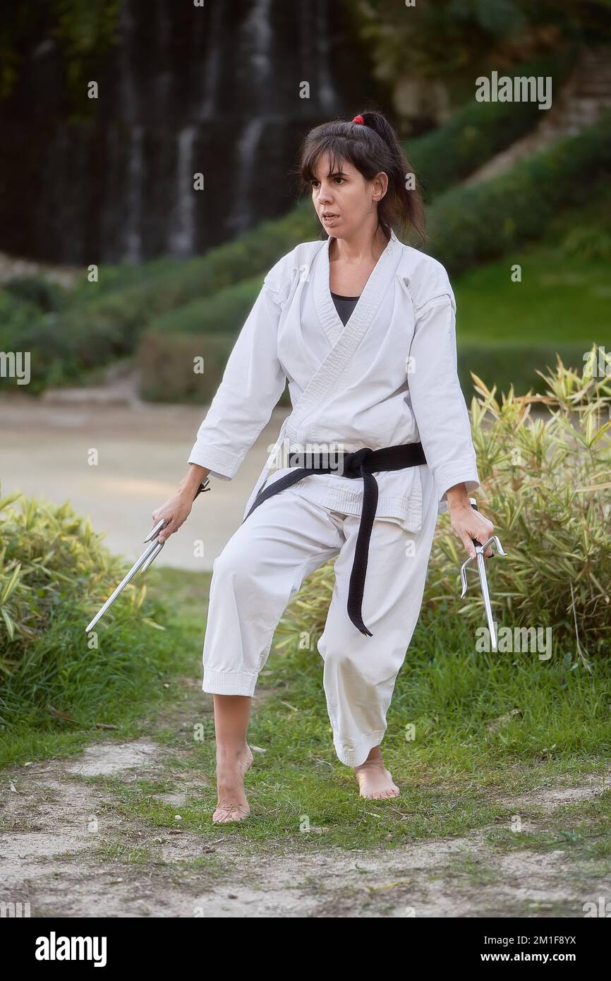 Young karate woman in fighting stance holding a pair of sai outdoors ...