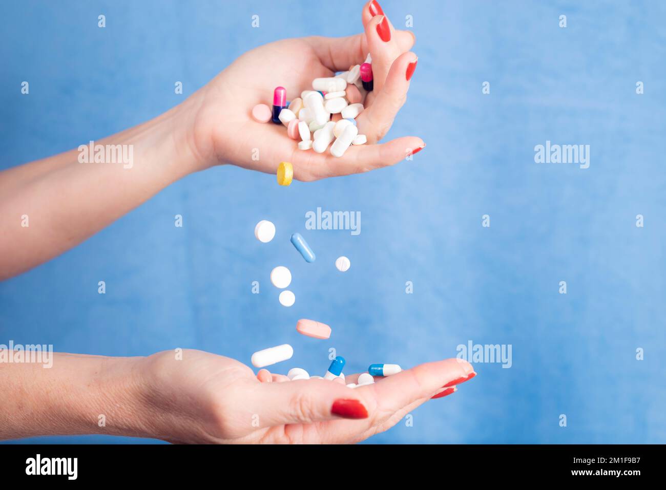 A several pills falling from one hand to another against blue ...