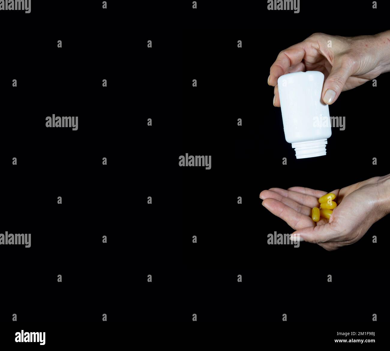 A hand pours yellow pills into the palm of another hand against a black ...