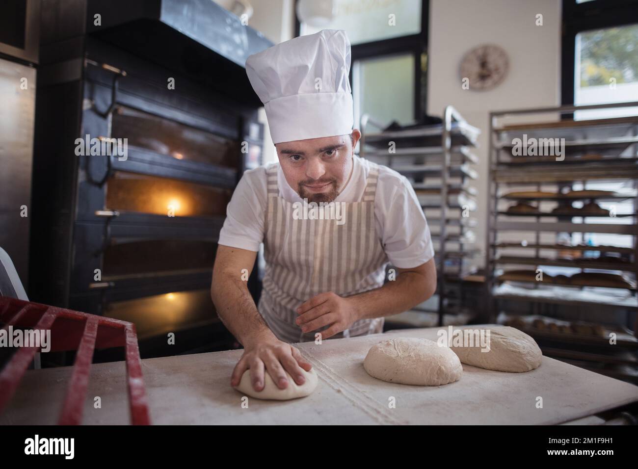 Young baker with down syndrome preparing pastries in bakery. Concept of ...