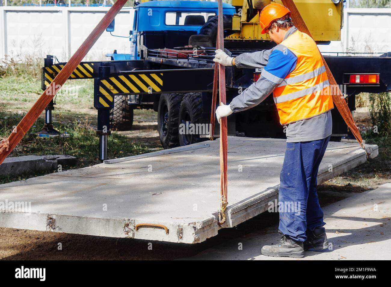 Slinger lays concrete slab on construction site on summer day. Worker ...