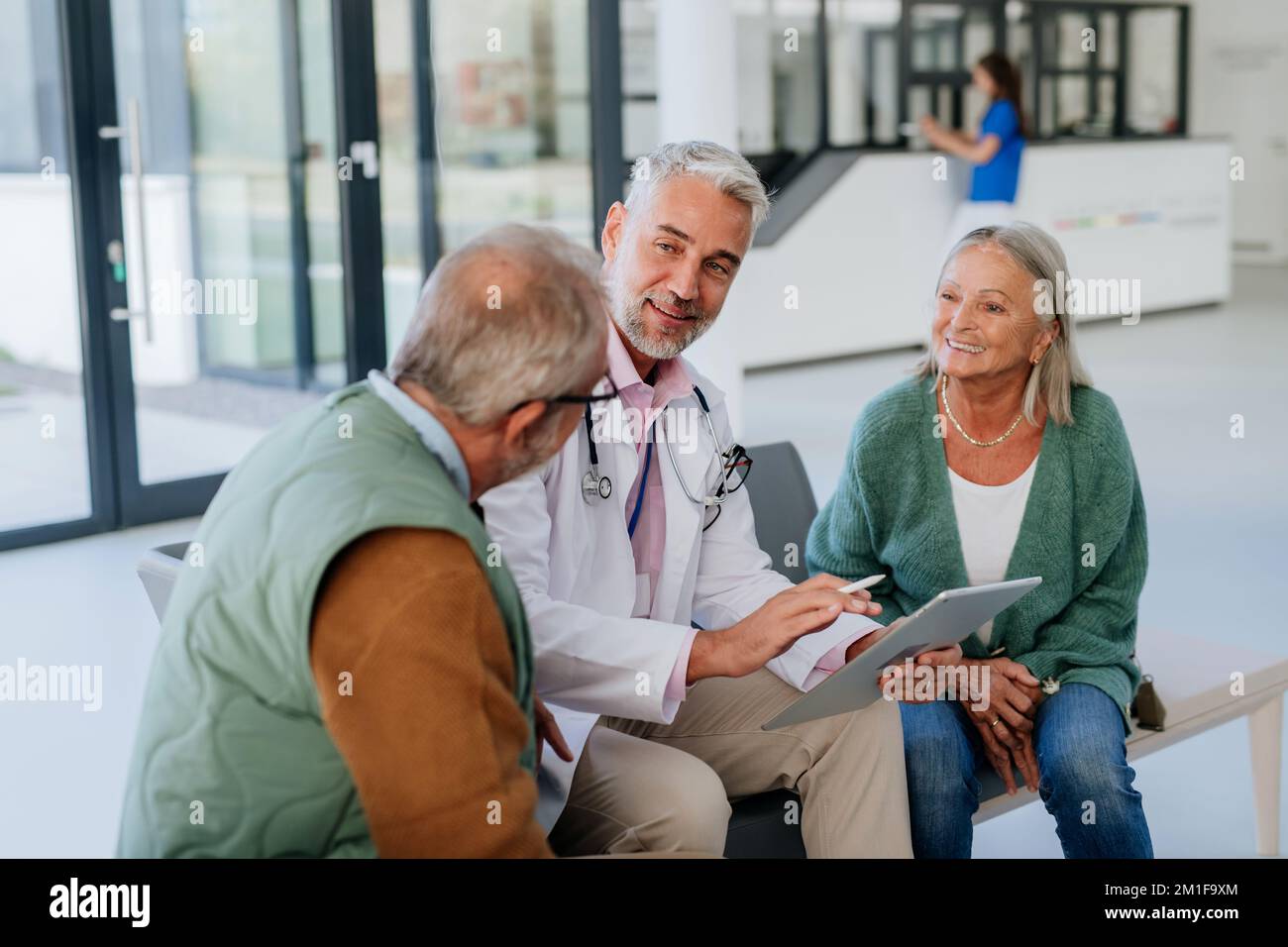 Mature doctor talking with his senior patients at hospital corridor ...