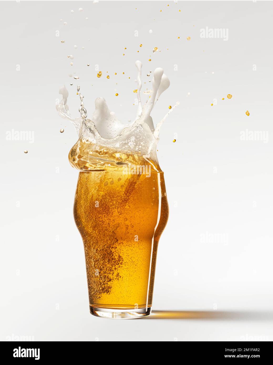 Ice cube falling down. Glass with chill foamy lager beer isolated over ...